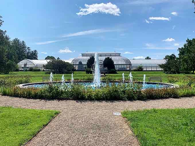A fountain centerpiece with greenhouse views beyond, combining water features with horticultural ambition in one elegant frame.