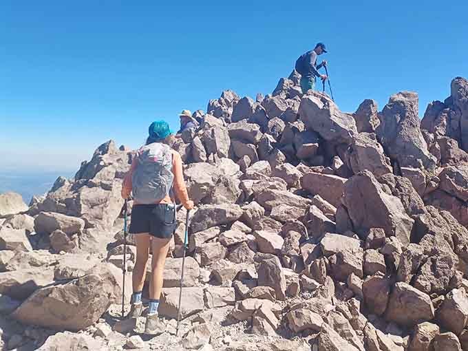 Fellow hikers scramble over volcanic rocks near the summit, united in their quest for bragging rights and Instagram glory.