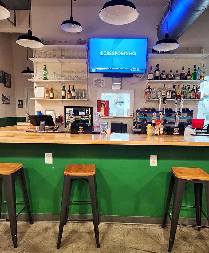That emerald green bar with wooden stools invites you to sit, sip, and watch the game in style.