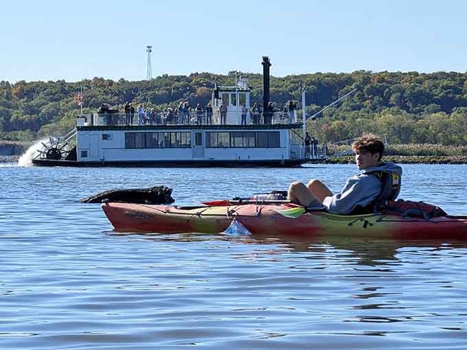 A kayaker drifts past a vintage paddlewheel boat, blending old-fashioned river romance with modern outdoor adventure perfectly.