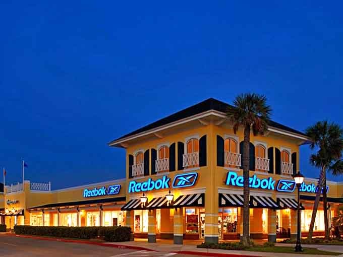Reebok glows against the twilight sky, its blue signage as electric as the feeling of finding sneakers at half price. Night shopping brings out the true bargain predators.