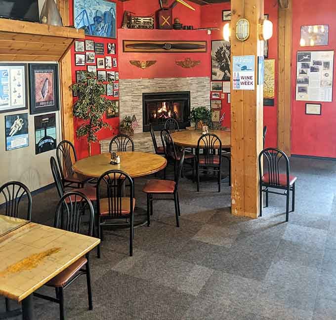 Fireplace warmth meets aviation history in this cozy dining space that somehow makes eating indoors feel like an adventure.