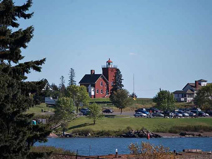 The red lighthouse perched on green grass creates a postcard moment that cameras simply cannot resist capturing.