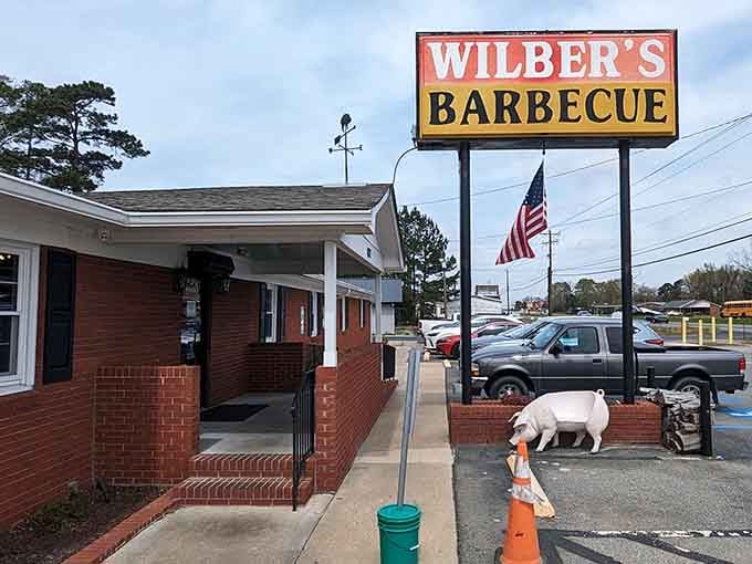 That proud American flag waves above a barbecue institution where the pig statue guards the entrance like a delicious sentinel.