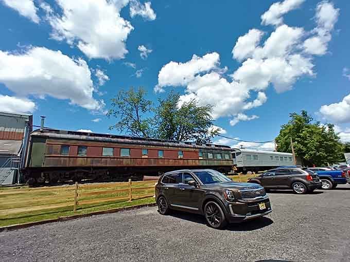 Modern cars meet vintage trains in a parking lot that bridges two centuries of American transportation dreams perfectly.
