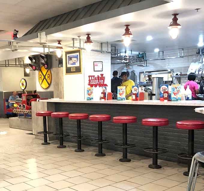 The counter area features classic diner stools and cheerful signage, where orders begin their journey to the overhead railway system.