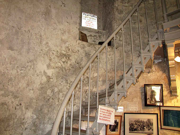 The base of the spiral staircase beckons visitors upward, with historic photos reminding you of the keepers who climbed daily.