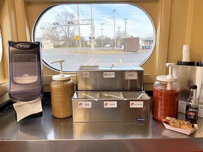 The condiment station with its oval window view, where mustard and ketchup wait patiently to fulfill their delicious destiny on your meal.