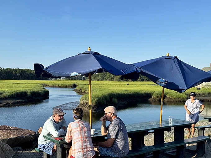 Blue umbrellas shade happy diners enjoying their feast with marsh breezes and waterfront views as the perfect seasoning.
