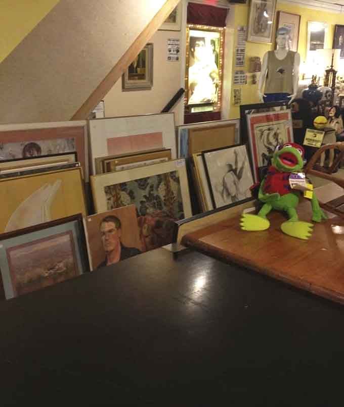 Framed art leans against tables like a gallery opening where everything's actually affordable and a stuffed frog photobombs the scene.