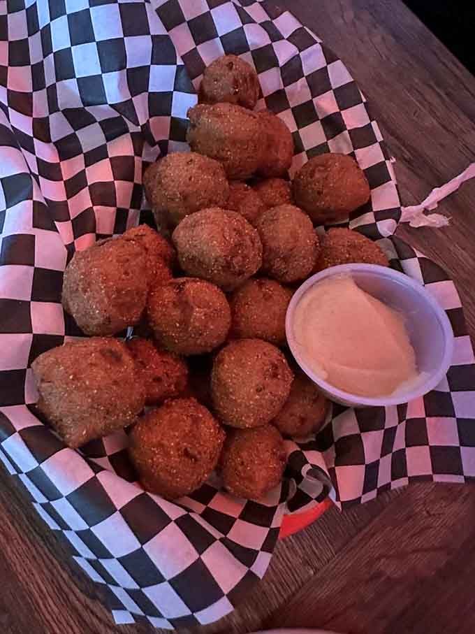 Golden hushpuppies piled high in checkered paper, served with creamy dipping sauce for maximum Southern satisfaction.