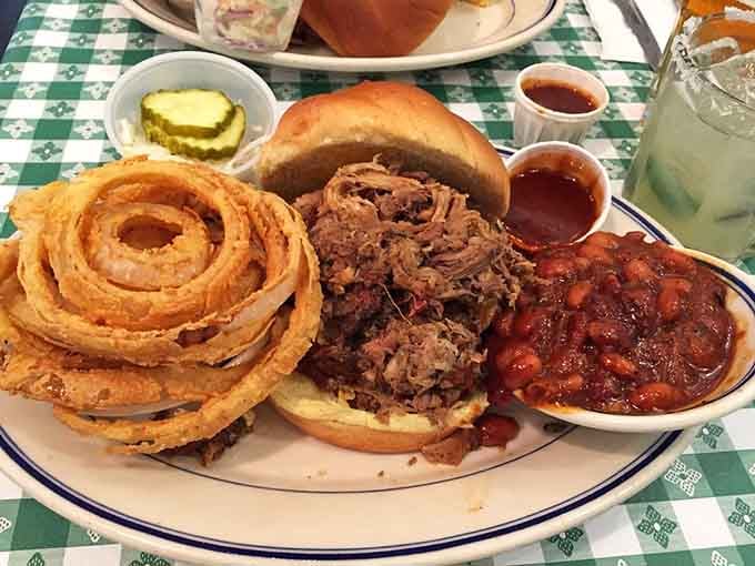 Pulled pork piled high with onion rings and baked beans creates a sandwich that requires strategic planning.