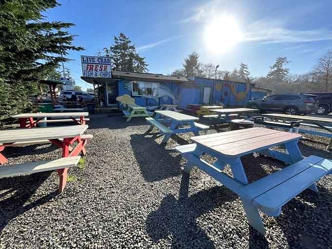 Colorful picnic tables dot the gravel lot under coastal sunshine, outdoor dining at its most unpretentious and utterly charming.