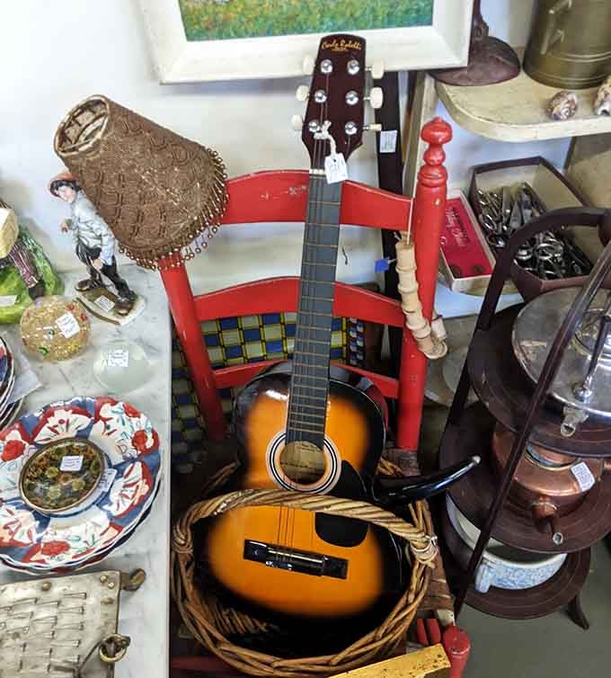 Strings attached! These vintage guitars wait silently for new hands to strum stories. Music instruments nestled among colorful chairs and forgotten treasures.