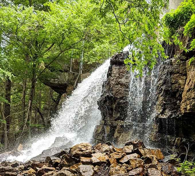 Water cascades dramatically over ancient rock formations. This hidden waterfall rewards hikers who venture beyond the beach crowds.