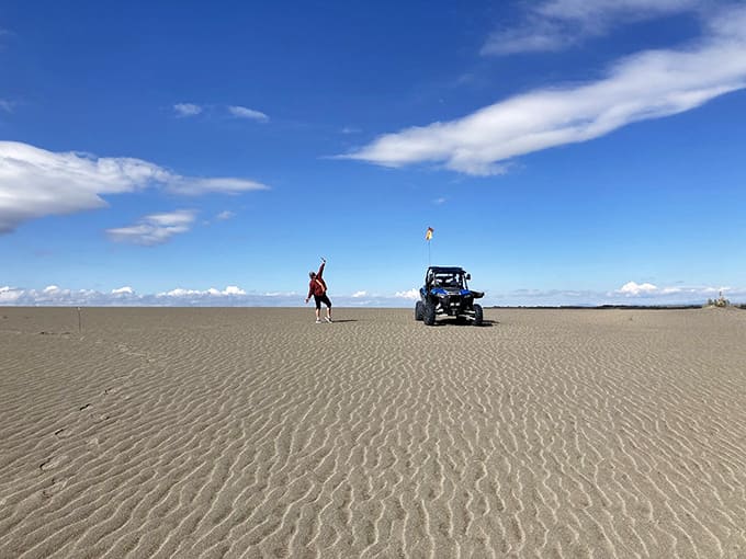 A visitor strikes a playful pose on the pristine sand, celebrating the otherworldly landscape stretching endlessly behind.