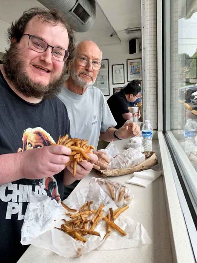 Pure joy captured: two generations united by hot dogs piled high with fries and zero regrets.