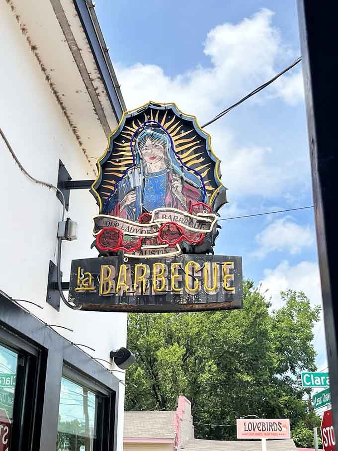 That iconic sign featuring Our Lady of Barbecue watches over the street, blessing all who seek smoked meat salvation below.