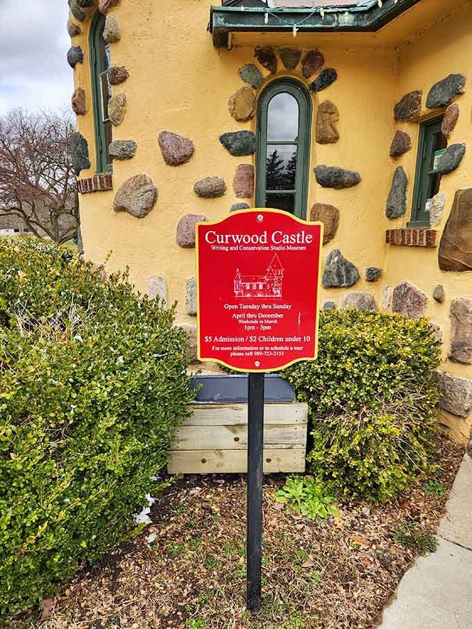 That cheerful red sign welcomes visitors to discover the castle where wilderness tales were born along Michigan's riverbanks.