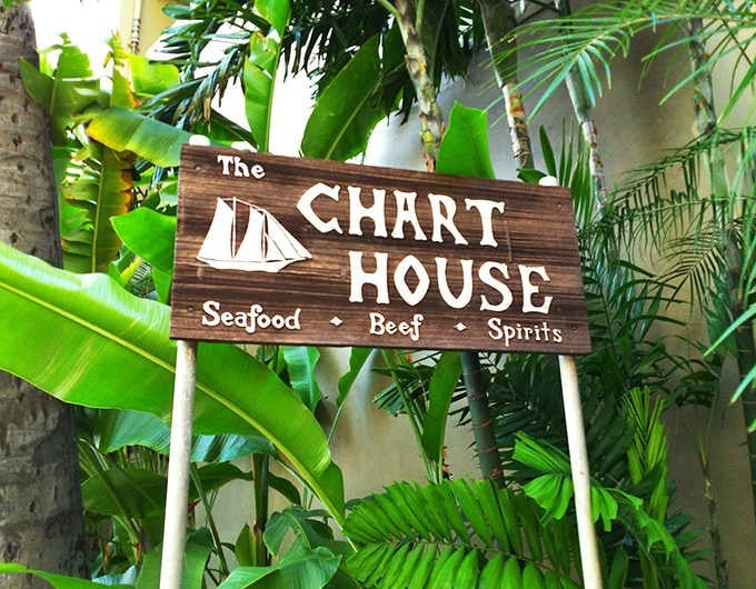 Nestled among tropical foliage, this wooden sign promises the holy trinity of vacation dining: seafood, beef, and spirits.