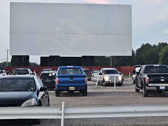 That towering white screen against the afternoon sky promises movie magic when darkness falls over the gravel lot.