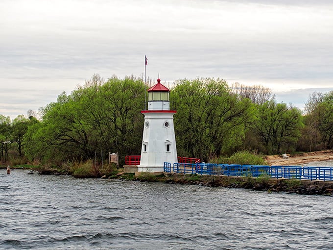 This charming lighthouse stands guard where river meets lake, its red cap bright against spring's green awakening.