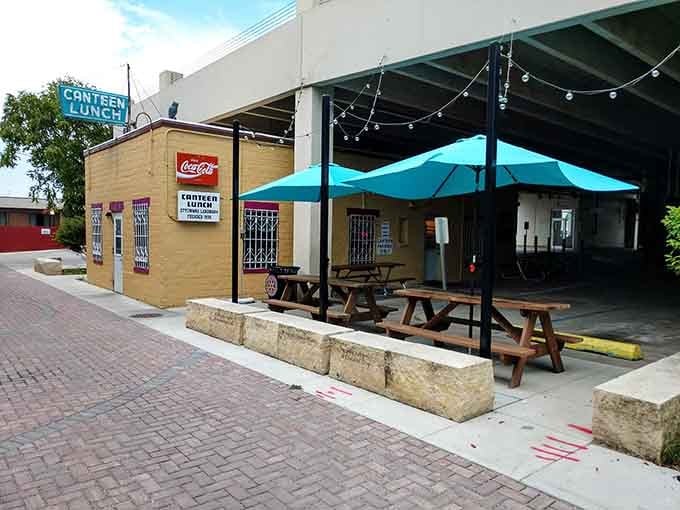 Outdoor picnic tables and blue umbrellas invite you to enjoy your loose meat sandwich in the alley's surprising charm.v