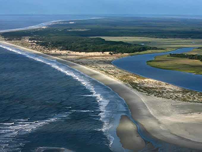 This sweeping barrier island curves like nature's perfect brushstroke, protecting marshlands teeming with coastal life and wonder.