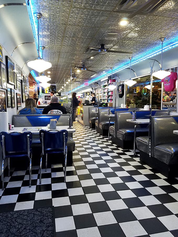 Classic Americana flows through every inch of this checkerboard paradise, where blue neon lighting transforms an ordinary ceiling into a retro-futuristic canopy over comfort food dreams.