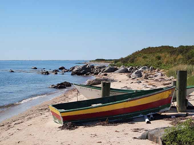 A rainbow rowboat rests on rocky shores, looking like it sailed straight out of a Winslow Homer painting.