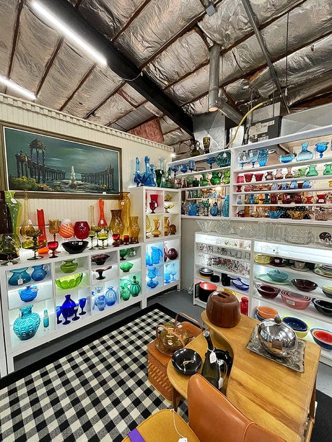 A symphony of colored glass catches light like musical notes. This meticulously organized collection transforms ordinary shelving into a kaleidoscopic wonderland of vintage glassware.