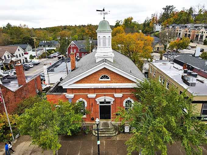 The historic brick building in Chagrin Falls stands proudly with its white steeple reaching skyward, surrounded by autumn's golden embrace.