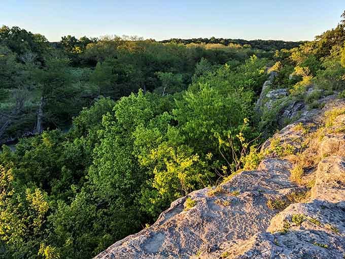 Golden hour light bathes the rocky overlook where Hill Country forests stretch endlessly toward the horizon below.