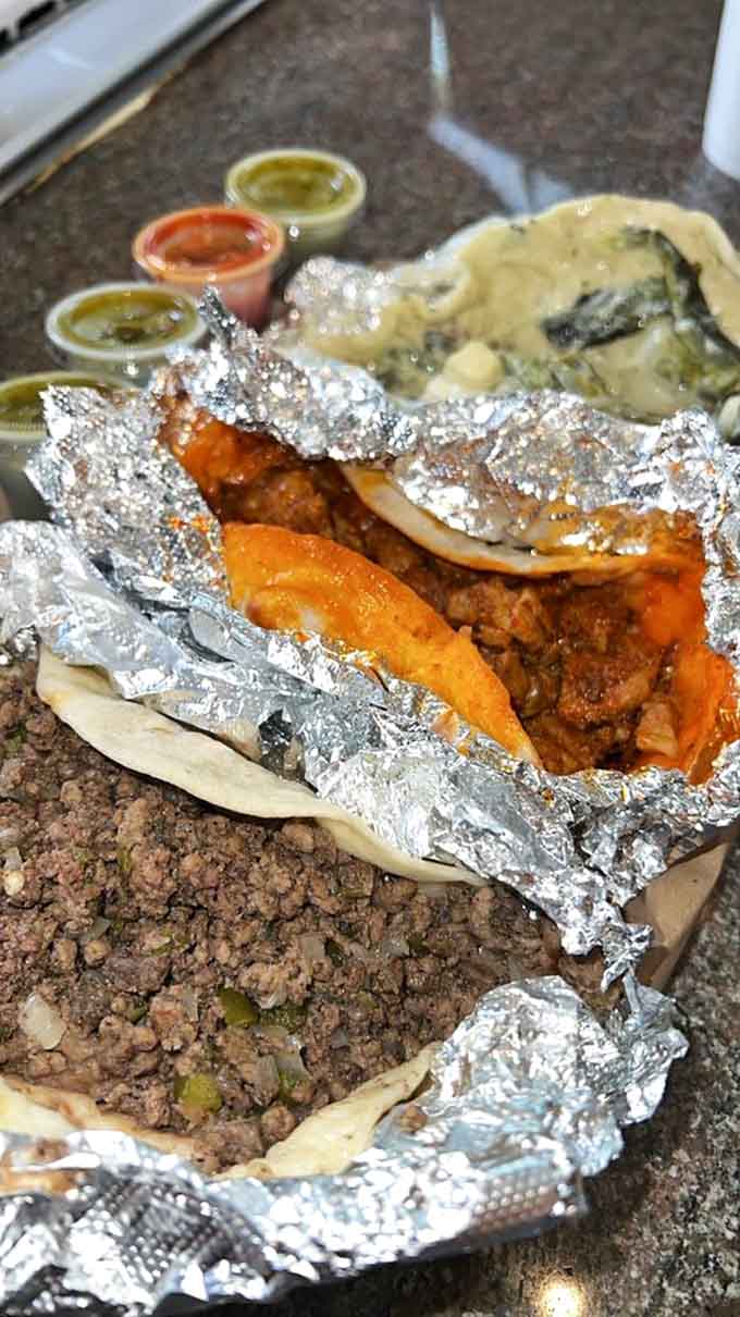 Foil-wrapped treasures reveal themselves like Christmas morning – spiced Al Pastor nestled beside ground beef, with three salsas standing by for duty.