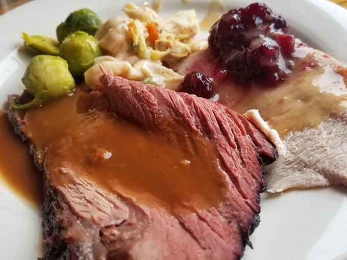 Tender baked ham draped in cider sauce sits alongside Brussels sprouts, proving vegetables can join the party.