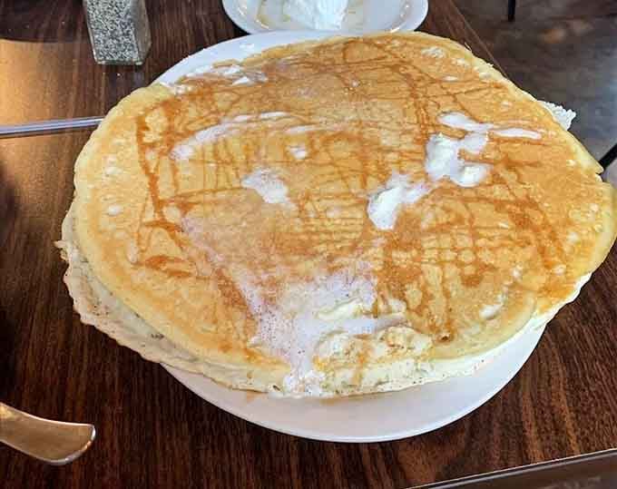 Behold the pancake that could double as a dinner plate—fluffy, golden, and dusted with powdered sugar perfection.