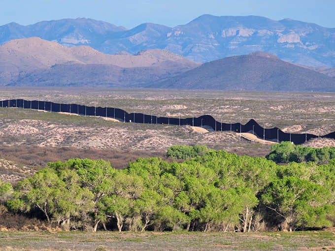 The border fence stretches across the landscape, a man-made divider in nature's seamless canvas of mountains and sky.