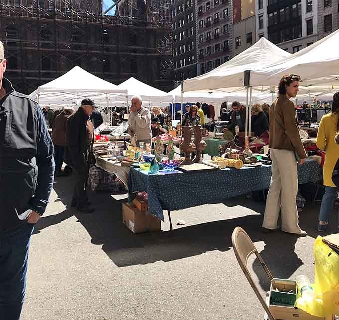 Urban buildings tower overhead while white tents shelter tables brimming with vintage treasures and handmade goods.