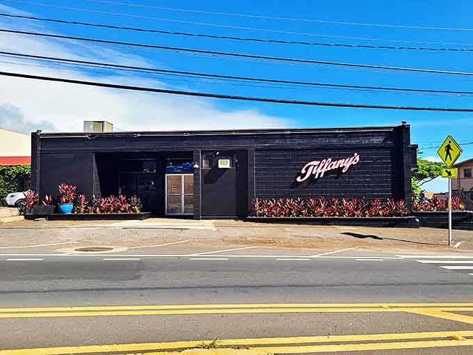 Tiffany's sleek black exterior stands out along the roadside. The vibrant red plants offer a hint of the bold flavors waiting inside.