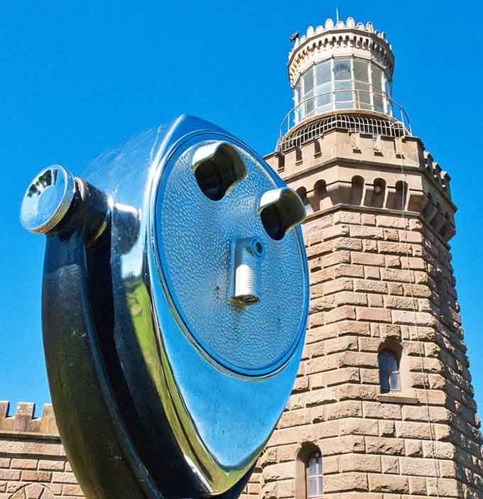 The vintage viewing scope points toward the brownstone tower, offering visitors a closer look at this unique lighthouse design.
