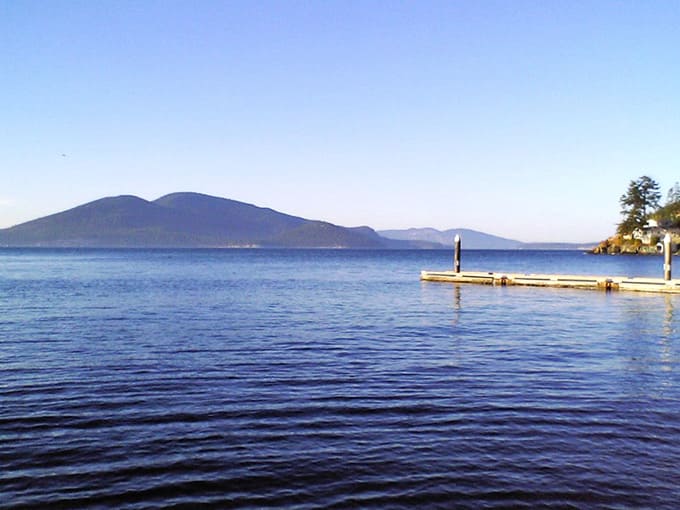 That wooden dock stretching toward distant mountains whispers promises of peaceful mornings and spectacular sunsets ahead.