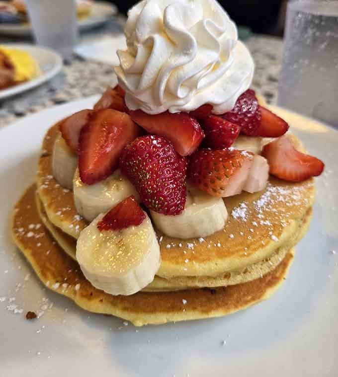 Strawberries, bananas, and whipped cream piled high on golden pancakes, because subtlety has no place at breakfast here.