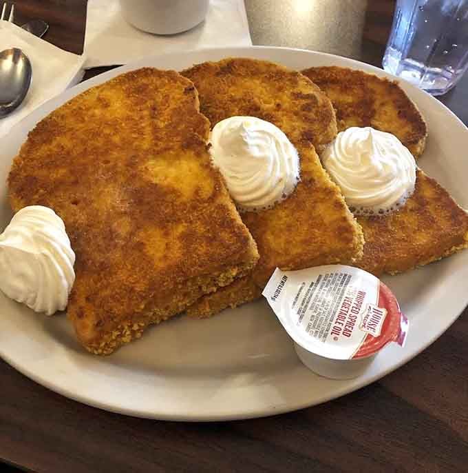 French toast done right: thick slices with a golden crust, crowned with whipped cream rosettes like edible architecture.