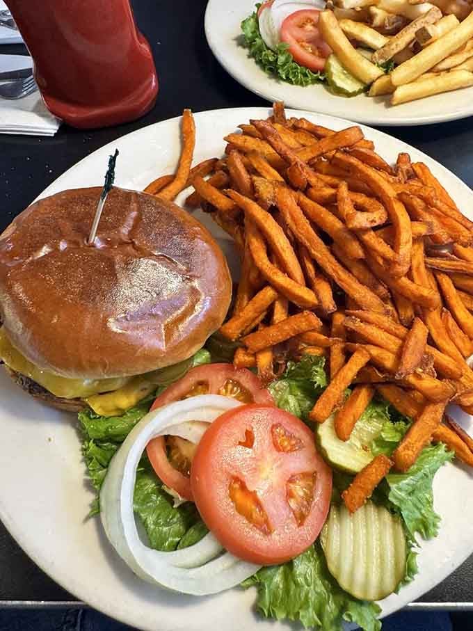 That burger comes with sweet potato fries piled high enough to require architectural planning and serious appetite commitment.