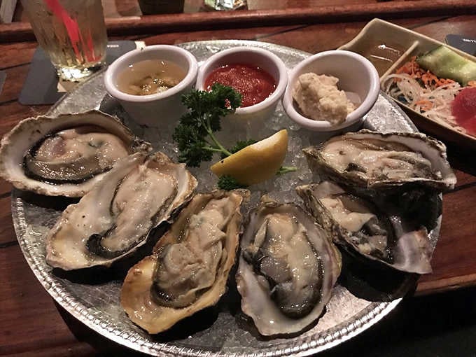 Fresh oysters arrive like jewels on a silver platter, accompanied by the traditional trinity of mignonette, cocktail sauce, and horseradish.