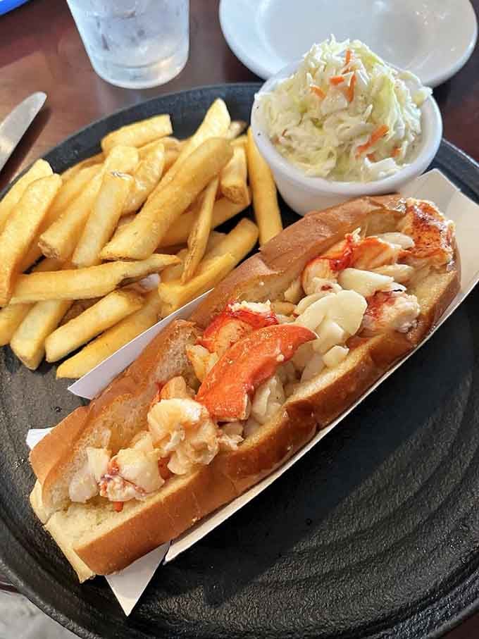 This lobster roll overflows with sweet meat, accompanied by golden fries and crisp coleslaw for the complete coastal experience.