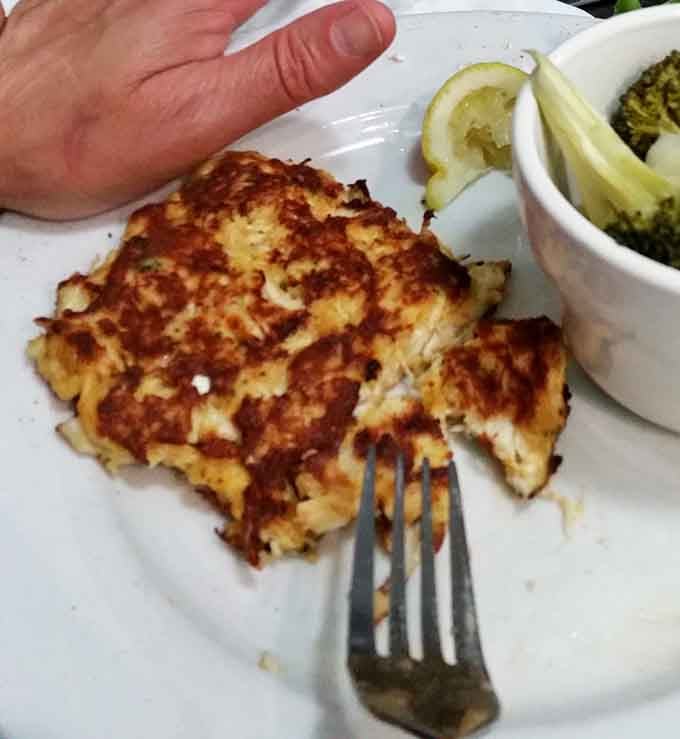 A hand for scale reveals these aren't dainty appetizers; this is the kind of crab cake that means business.