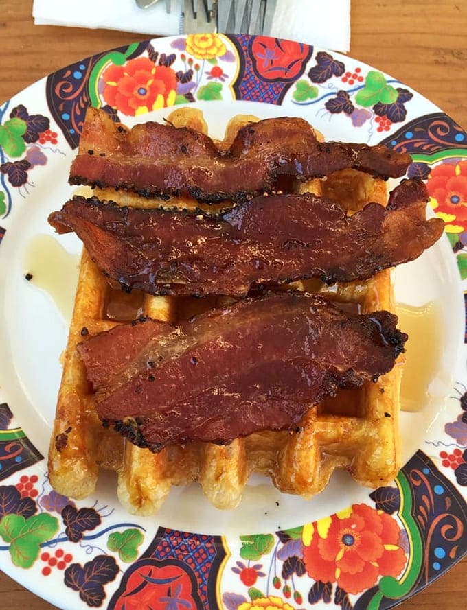 Thick-cut bacon draped over a crispy waffle with maple syrup, proving breakfast doesn't need to be complicated.