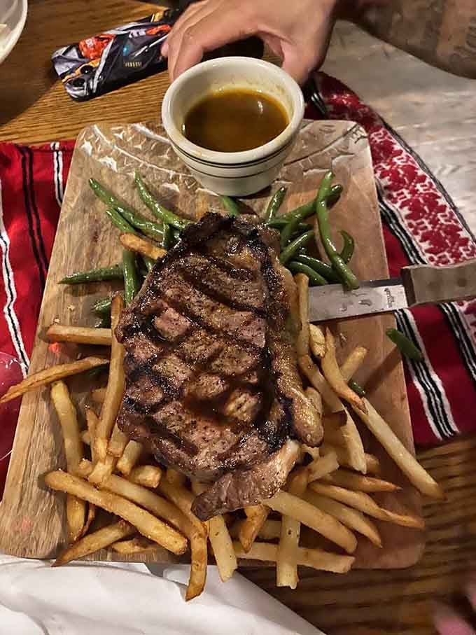 That perfectly grilled steak arrives on a wooden board like edible artwork, surrounded by crispy fries and fresh vegetables.