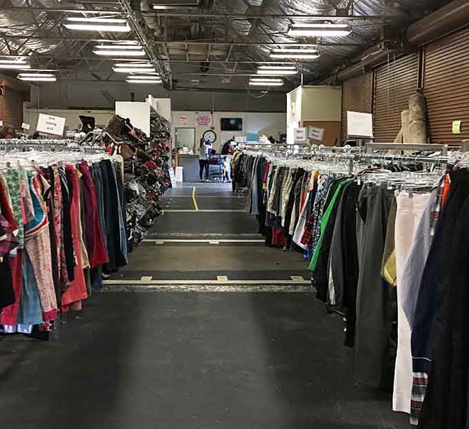 Rows of colorful clothing stretch endlessly under industrial lighting, creating a rainbow pathway for determined thrift shoppers.